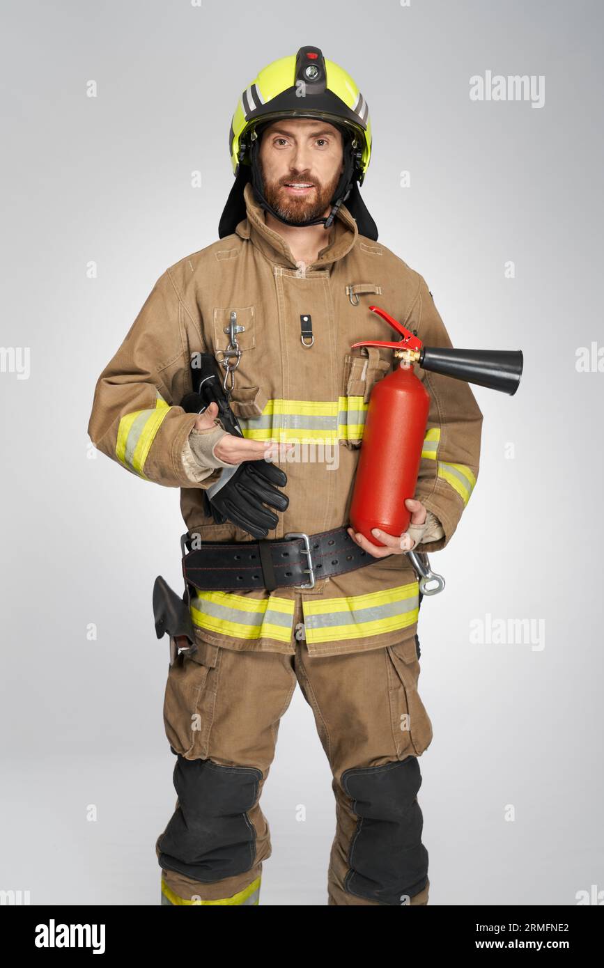 Handsome firefighter presenting fire extinguisher in studio. Portrait ...