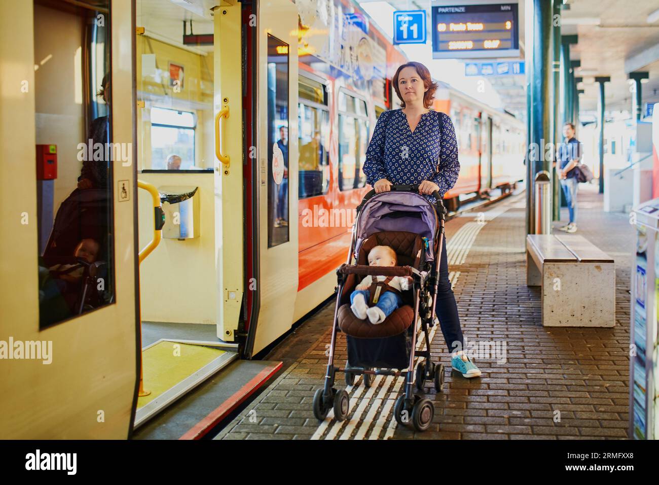 Woman with little girl in stroller at railway station. Mother with baby ...