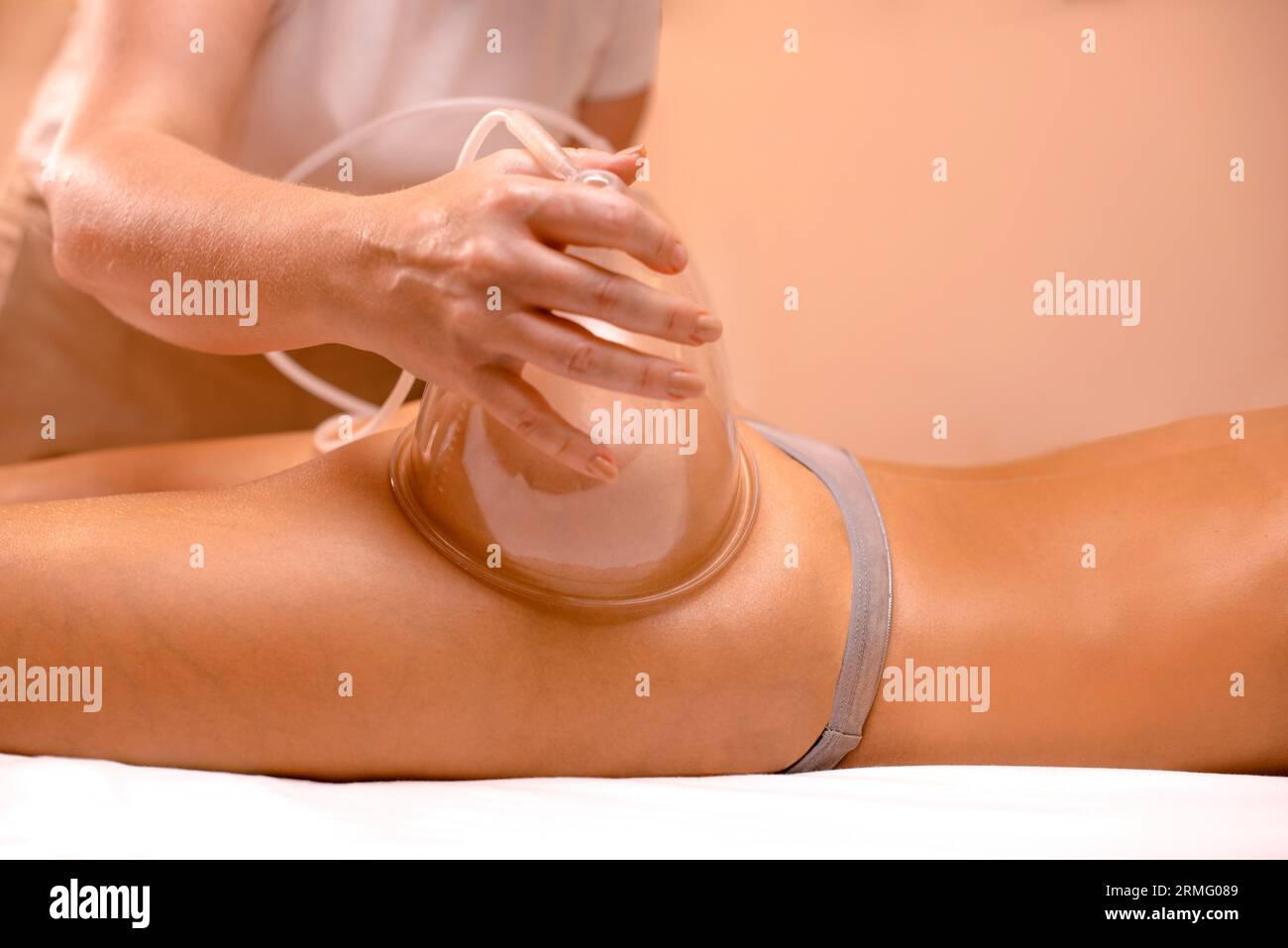 Doctor performing vacuum therapy treatment for buttocks lifting on female patient in medical ...
