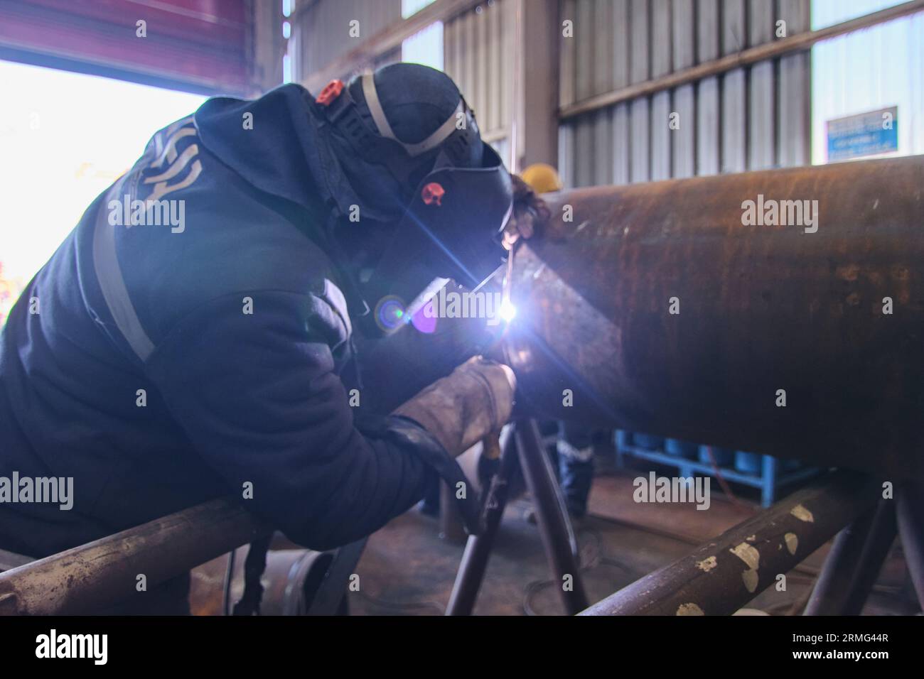a man in full safety gear like a helmet, visor, and vest. doing welding ...