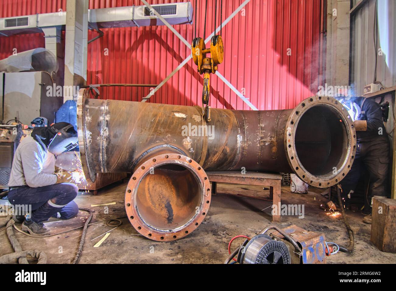 a man in full safety gear like a helmet, visor, and vest. doing welding ...