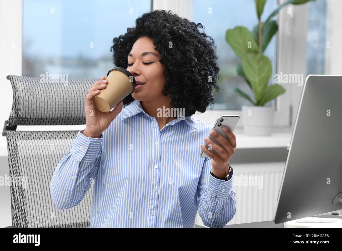 Young woman drinking coffee while working on computer in office Stock ...