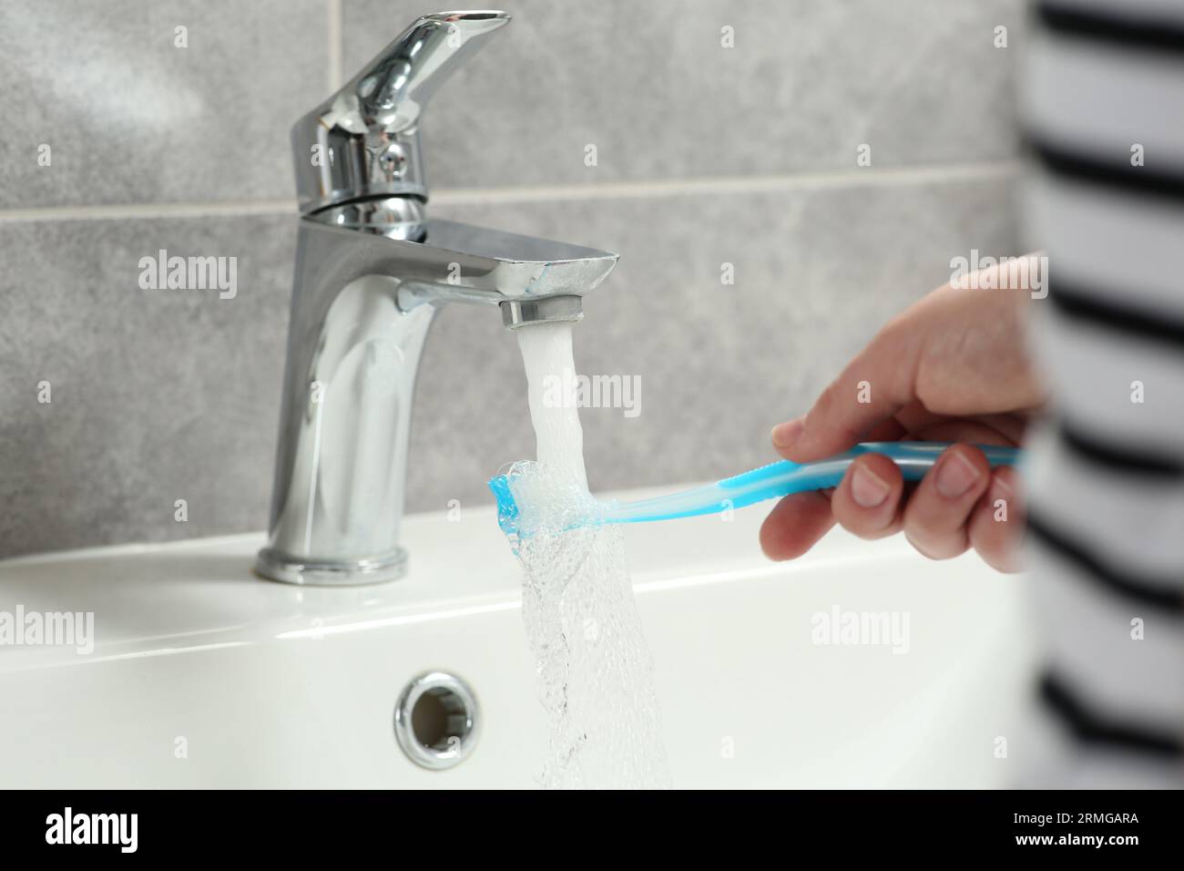 Woman washing plastic toothbrush under flowing water from faucet in ...