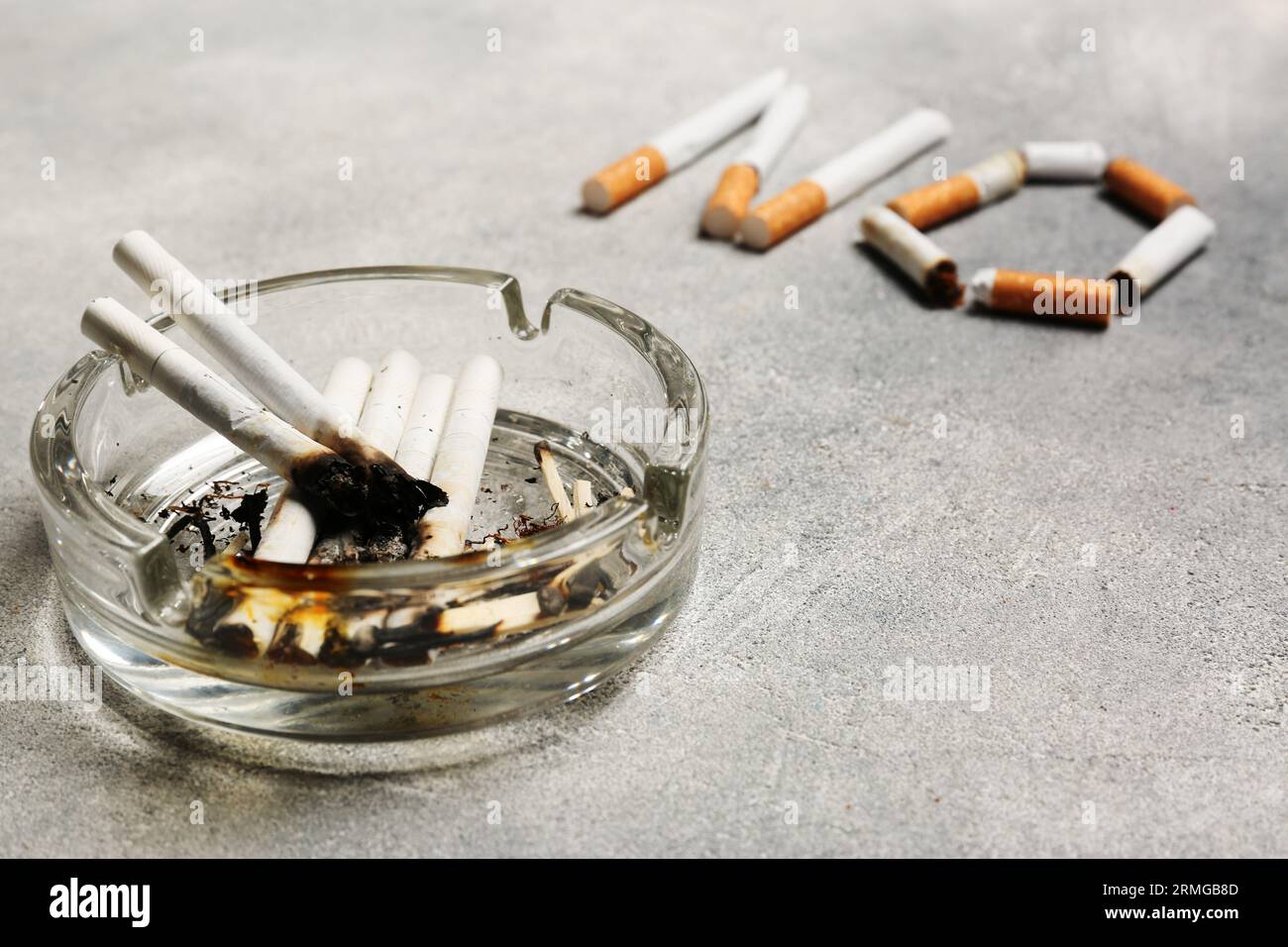 Ashtray with burnt butts and word No made of cigarettes on grey table ...