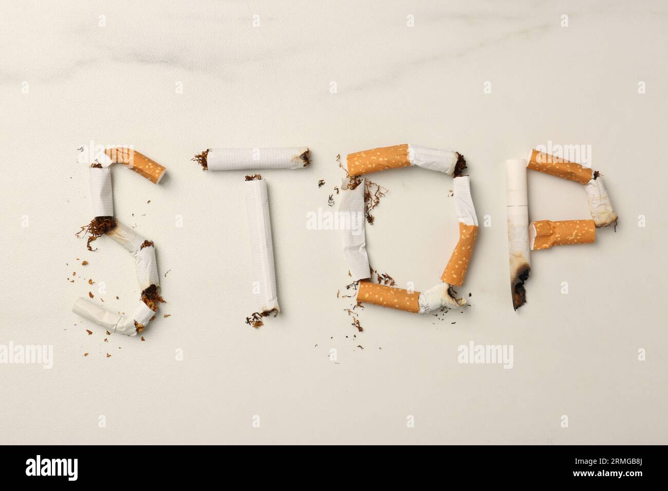 Word Stop made with burnt cigarettes on white marble table, flat lay ...