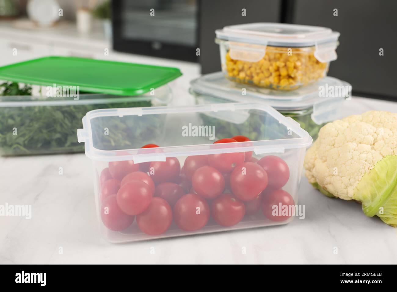 Containers with cherry tomatoes and fresh products on white marble ...