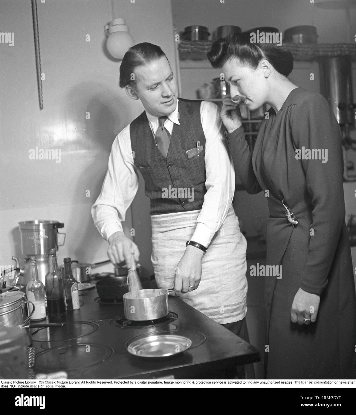 In the 1940s. A man at the kitchen stove making something in a saucepan ...