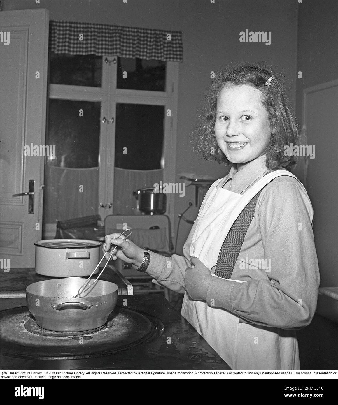 In the 1940s. A girl at the cooker with a pan that she has something ...