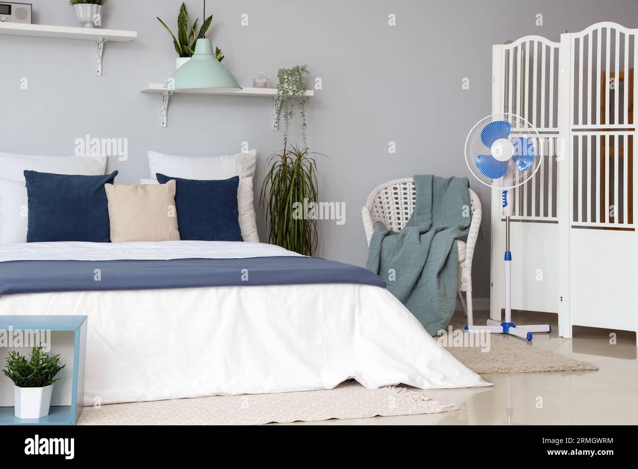 Interior of light bedroom with cozy bed and floor fan Stock Photo - Alamy