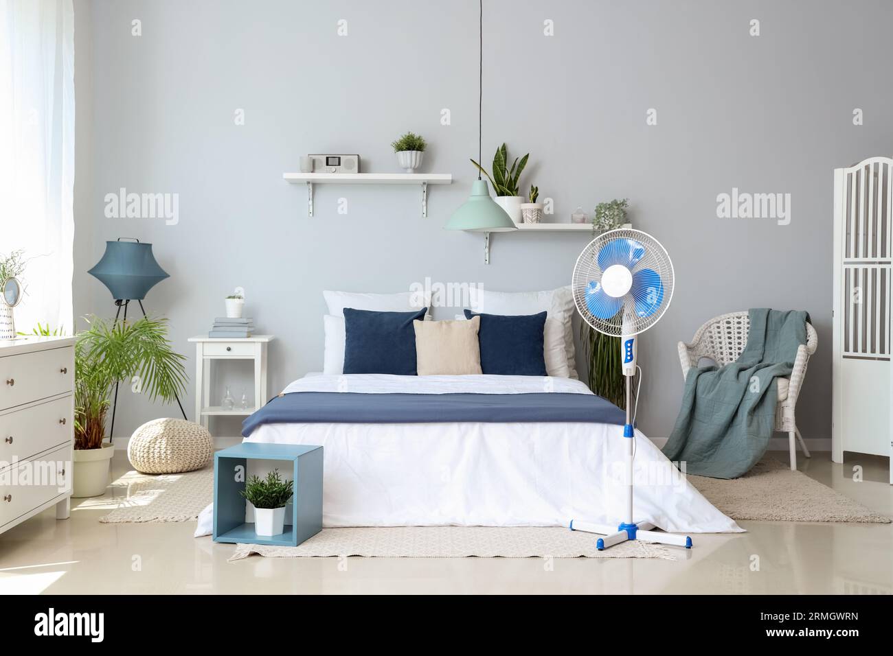Interior of light bedroom with cozy bed and floor fan Stock Photo - Alamy