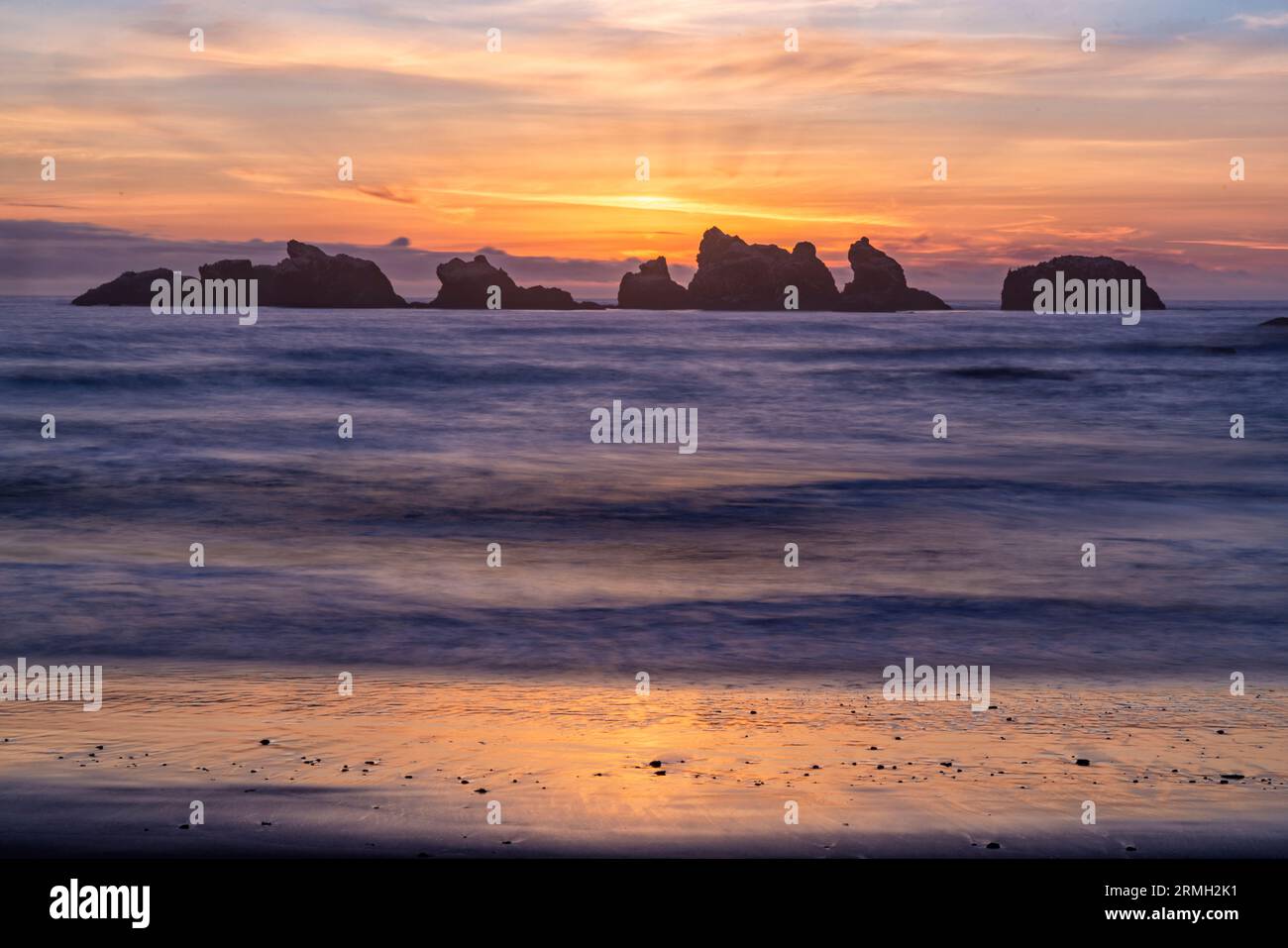 A colorful sky lingers behind sea stacks, behind long exposure waves on ...