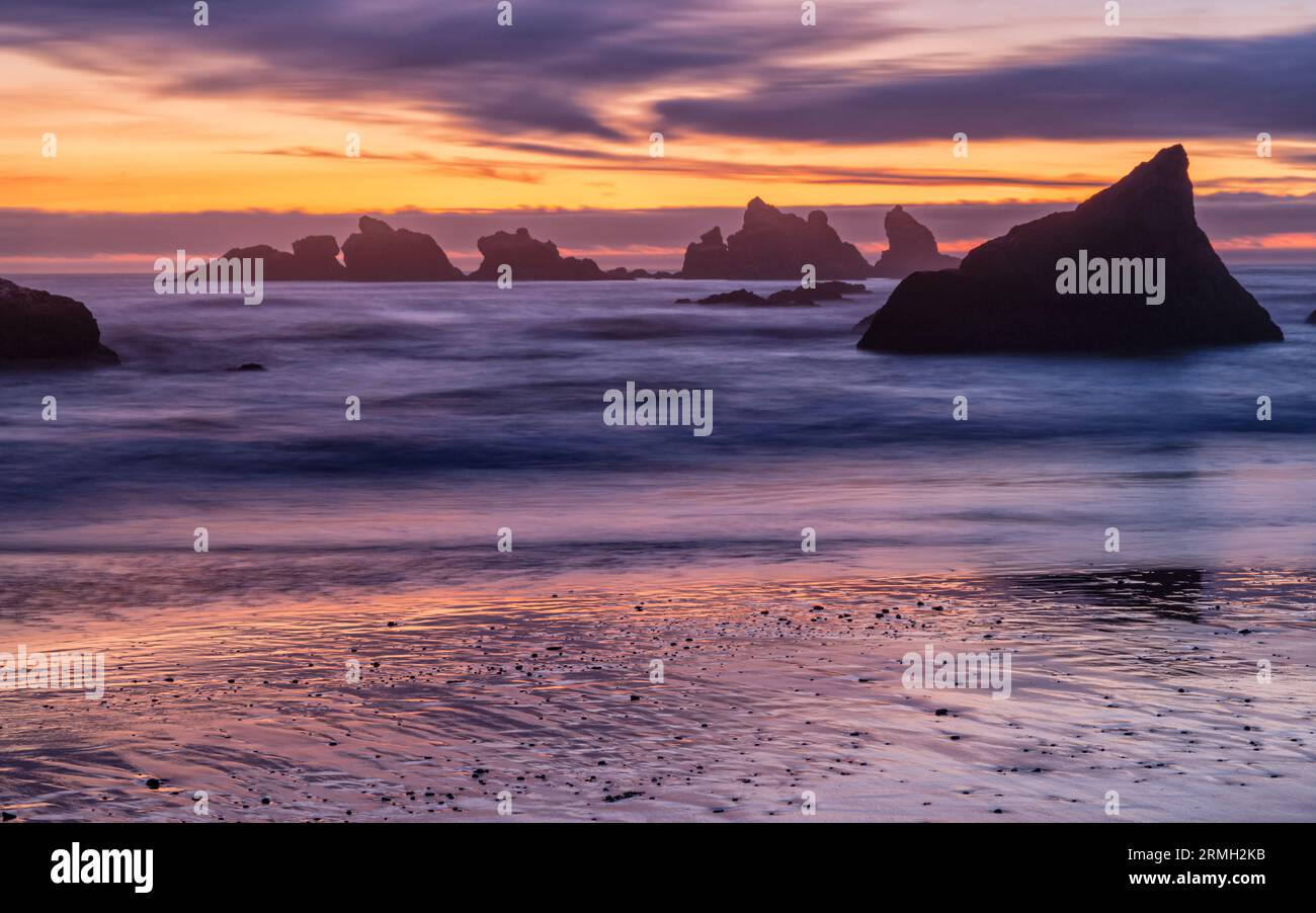 Wet sand looks metallic as it reflects a colorful post sunset sky, with ...