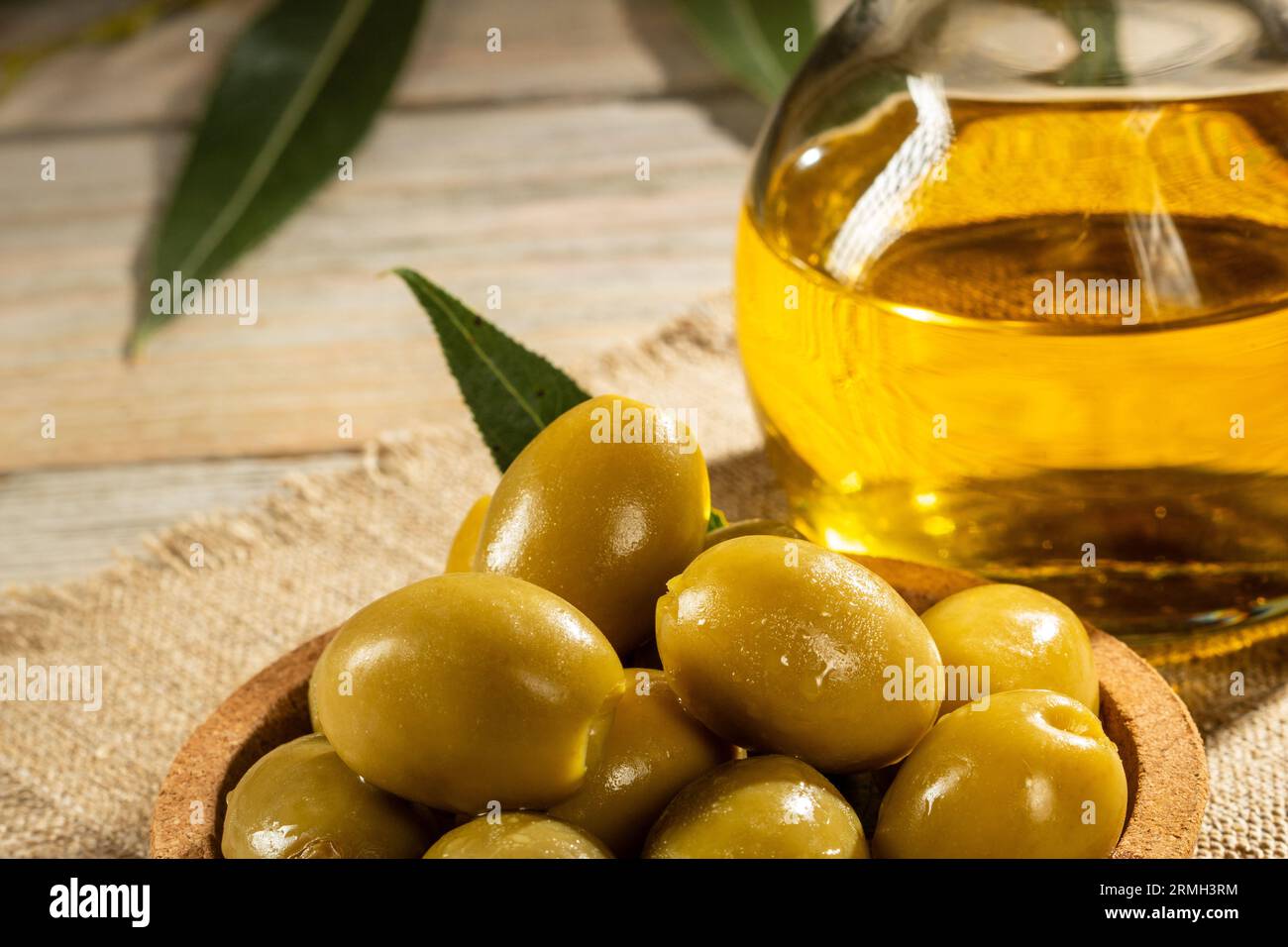 A bunch of green olives and a jug of olive oil on a burlap napkin ...