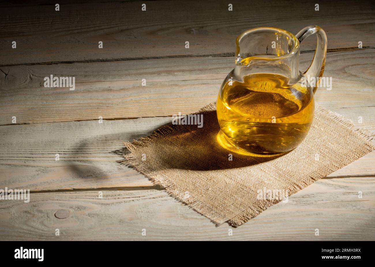 A glass jug of olive oil and a burlap napkin on a kitchen table ...