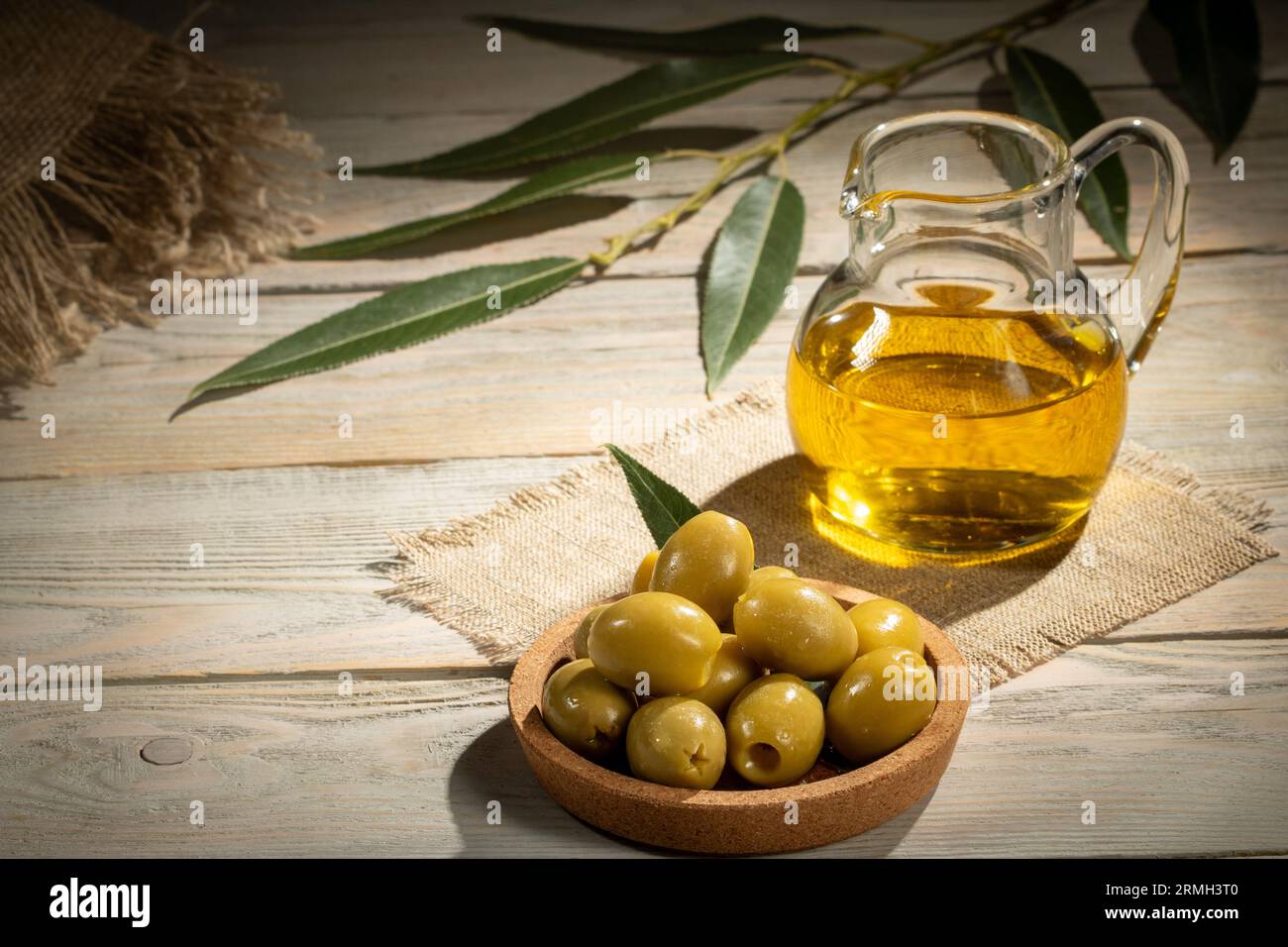 A bunch of green olives and a jug of olive oil on a burlap napkin ...