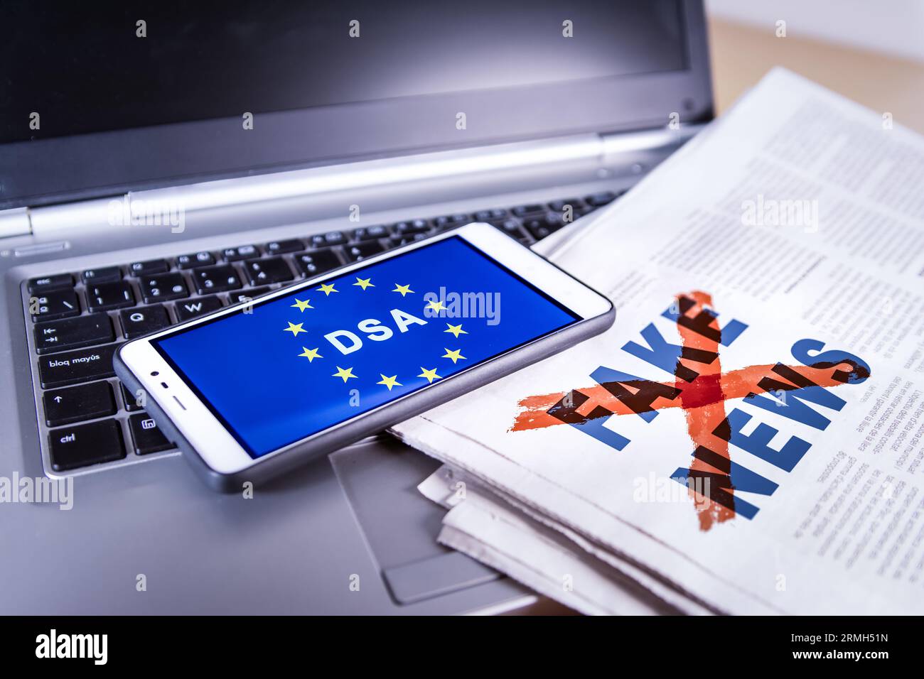 Smartphone with DSA and EU flag on screen over a newspaper with Fake news and a laptop. Fake ...