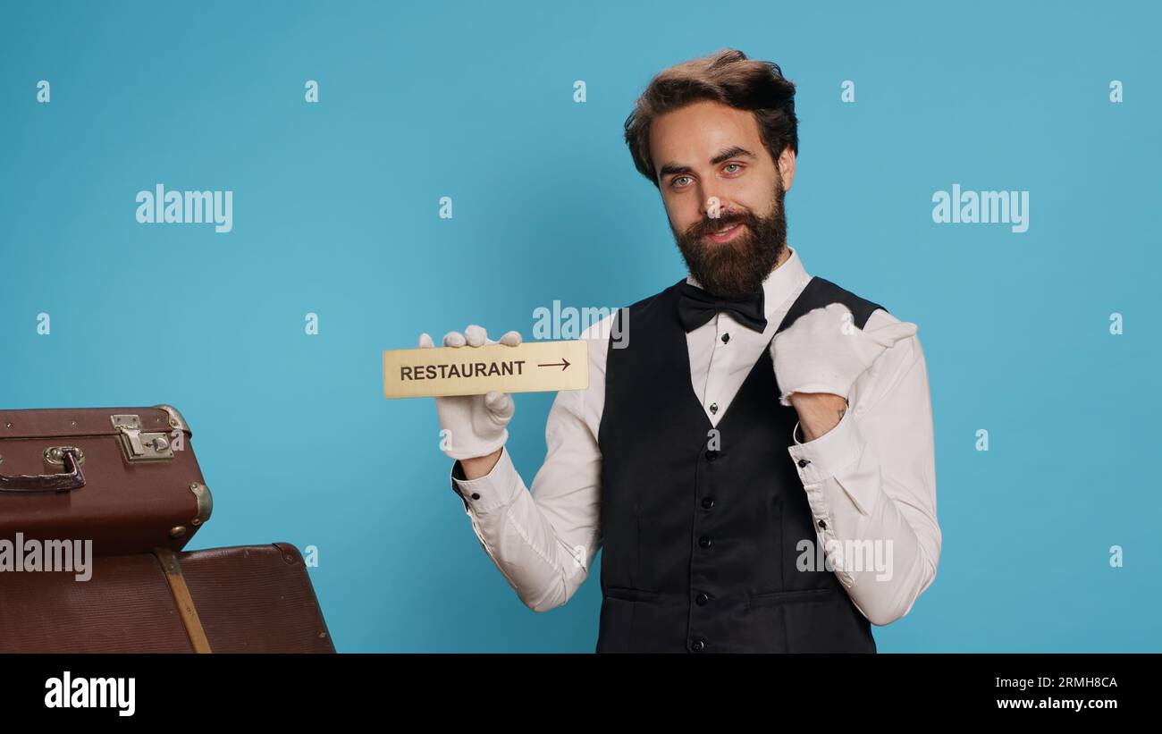 Hotel worker holds restaurant wall sign to help guests with directions ...