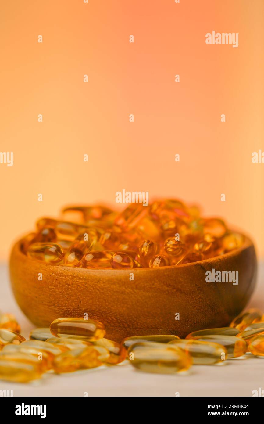Fish oil capsules in a wooden cup on a blurred orange background.Omega ...