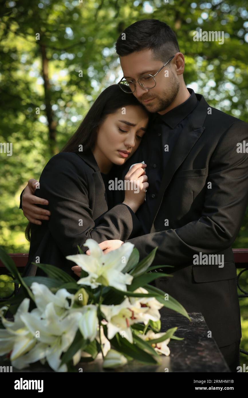 Sad couple mourning near granite tombstone with white lilies at ...