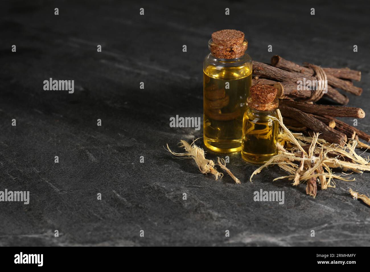 Dried sticks of licorice root and bottles with essential oil on black ...