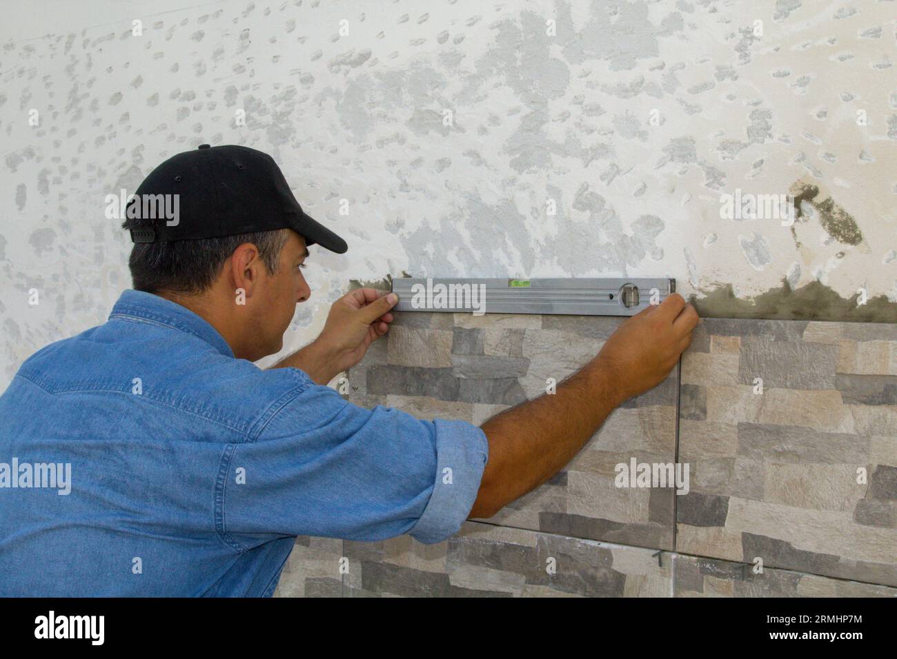 Image of a tiler who uses a spirit level to check and ensure that the ...