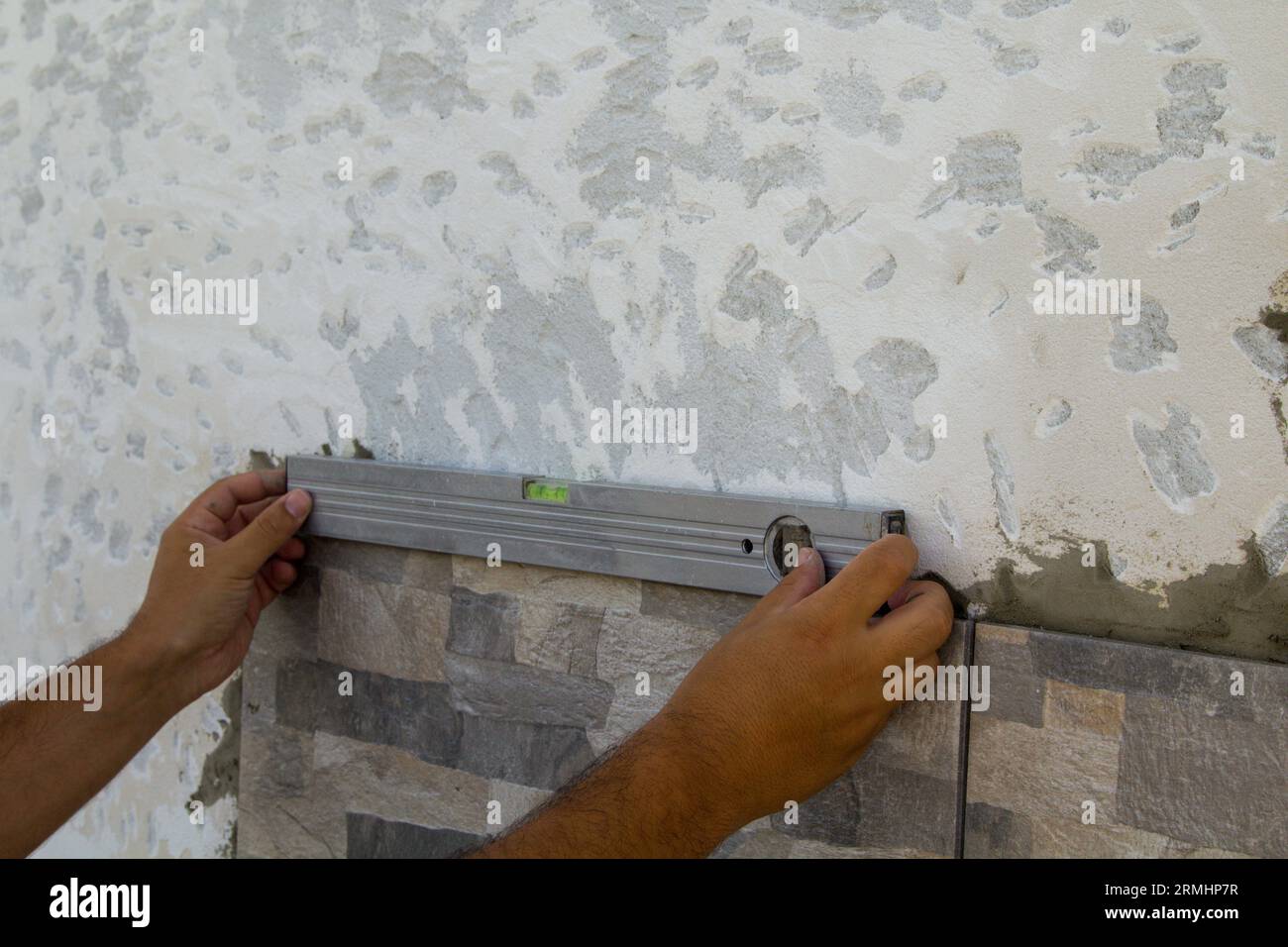 Image of the hands of a tiler while he checks the accuracy of the newly ...
