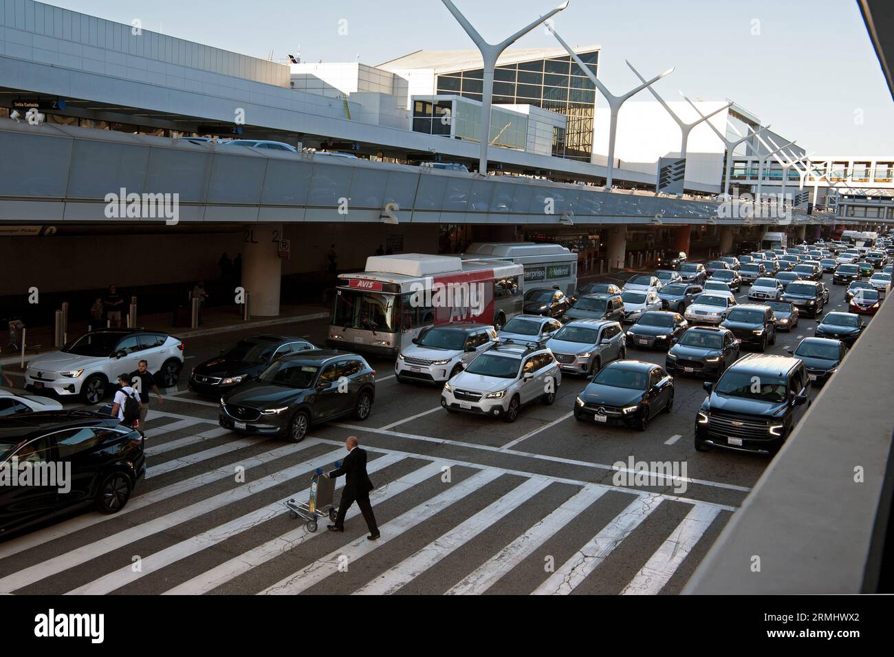 Heavy traffic in LAX stops for a man with luggage cart at a crosswalk ...