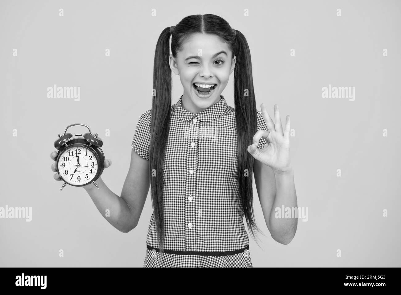 Child student girl with clock isolated on yellow background. Child back ...