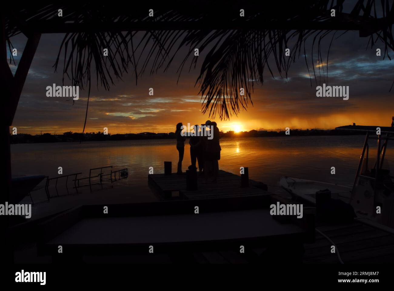 The silhouettes of 4 people standing on a pier at sunset on the Island ...