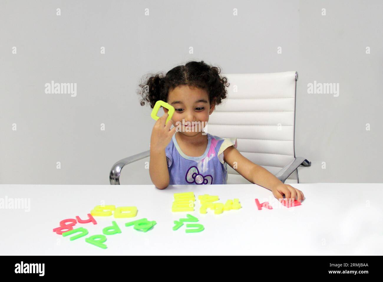 3-year-old brunette Latina girl plays with toy letters and numbers to ...