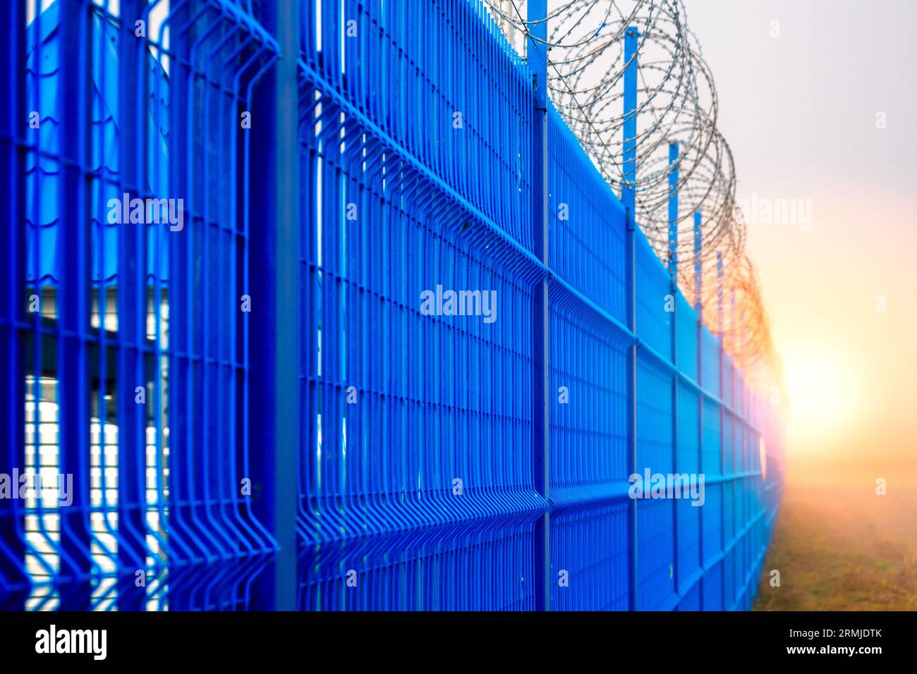 Blue metal fence with barbed wire on top. Fencing around perimeter ...
