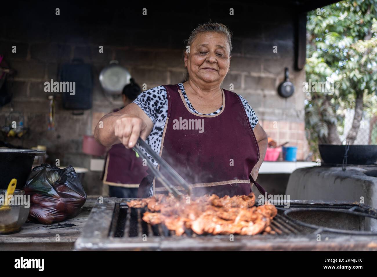 Portrait of a poor latin poor woman cooking meat on a grill. Nicaragua ...