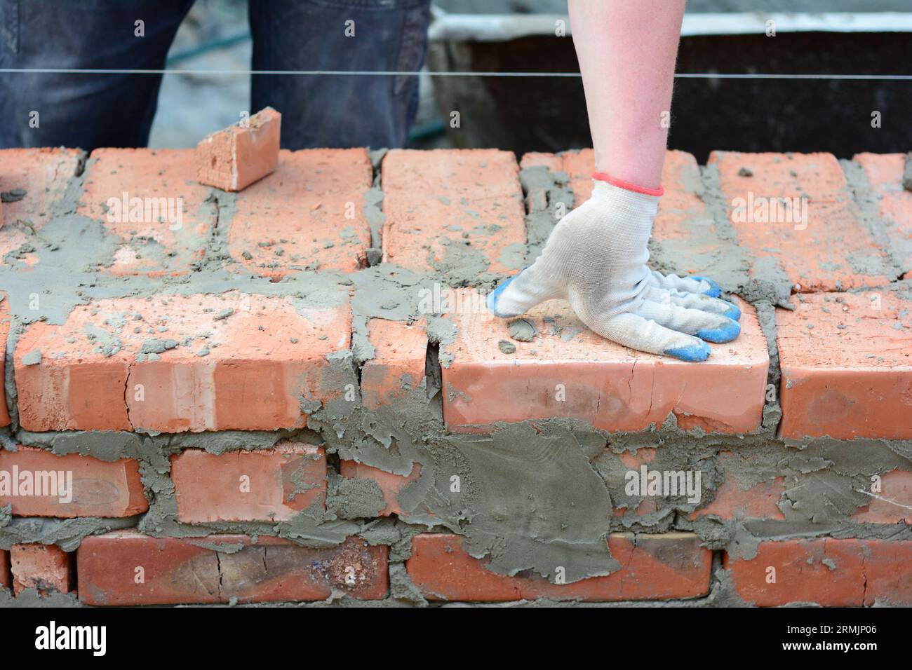 A mason person is building brick house wall. Close up on half bat and ...