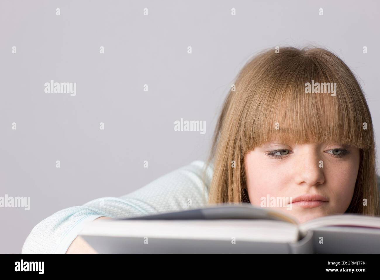 Young woman reading with face resting on book Stock Photo - Alamy
