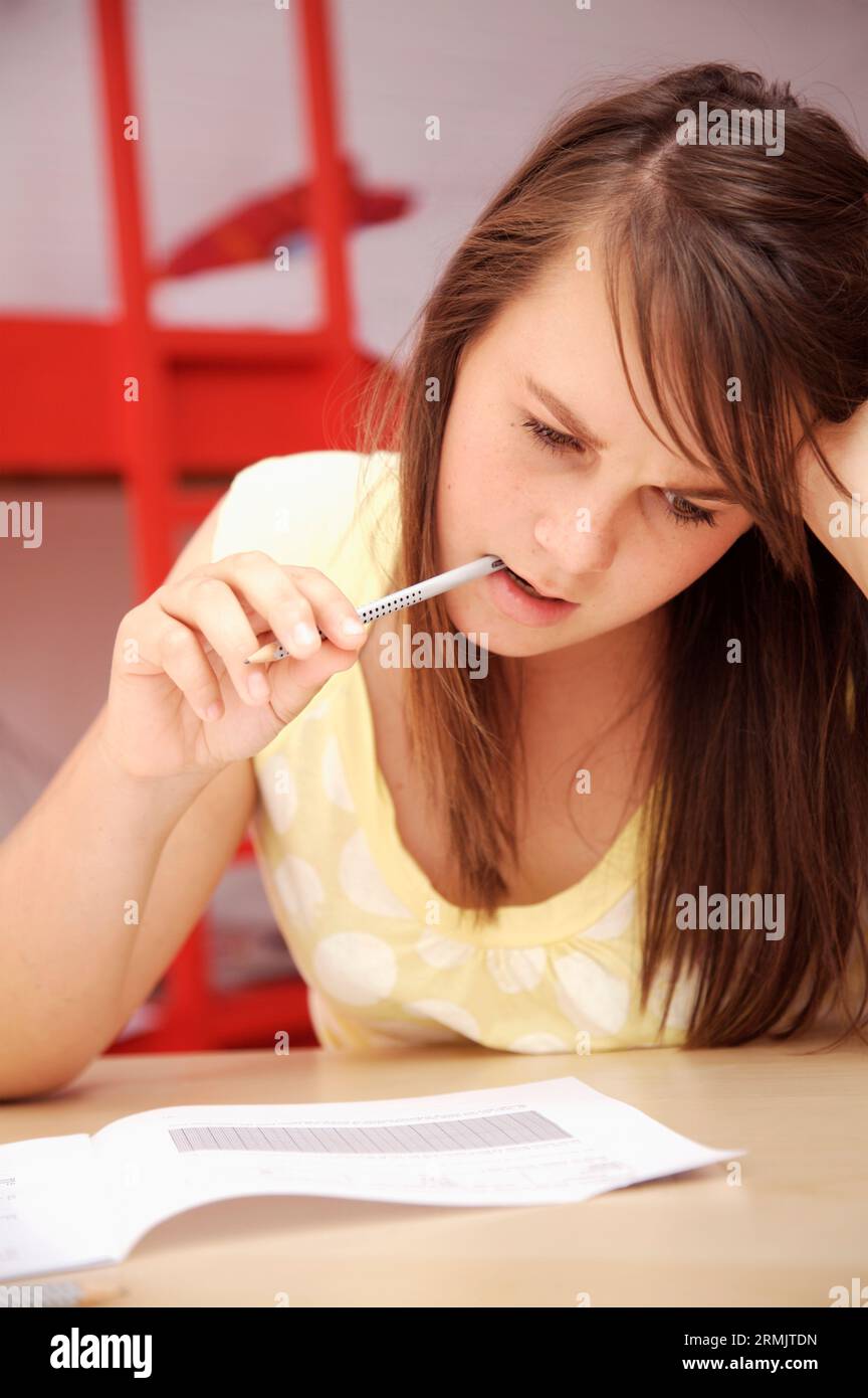 Young girl studying with pencil in mouth Stock Photo - Alamy