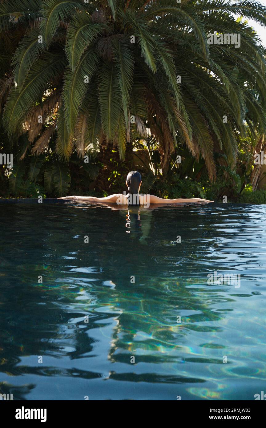Back of young woman standing in an exotic swimming pool with arms ...