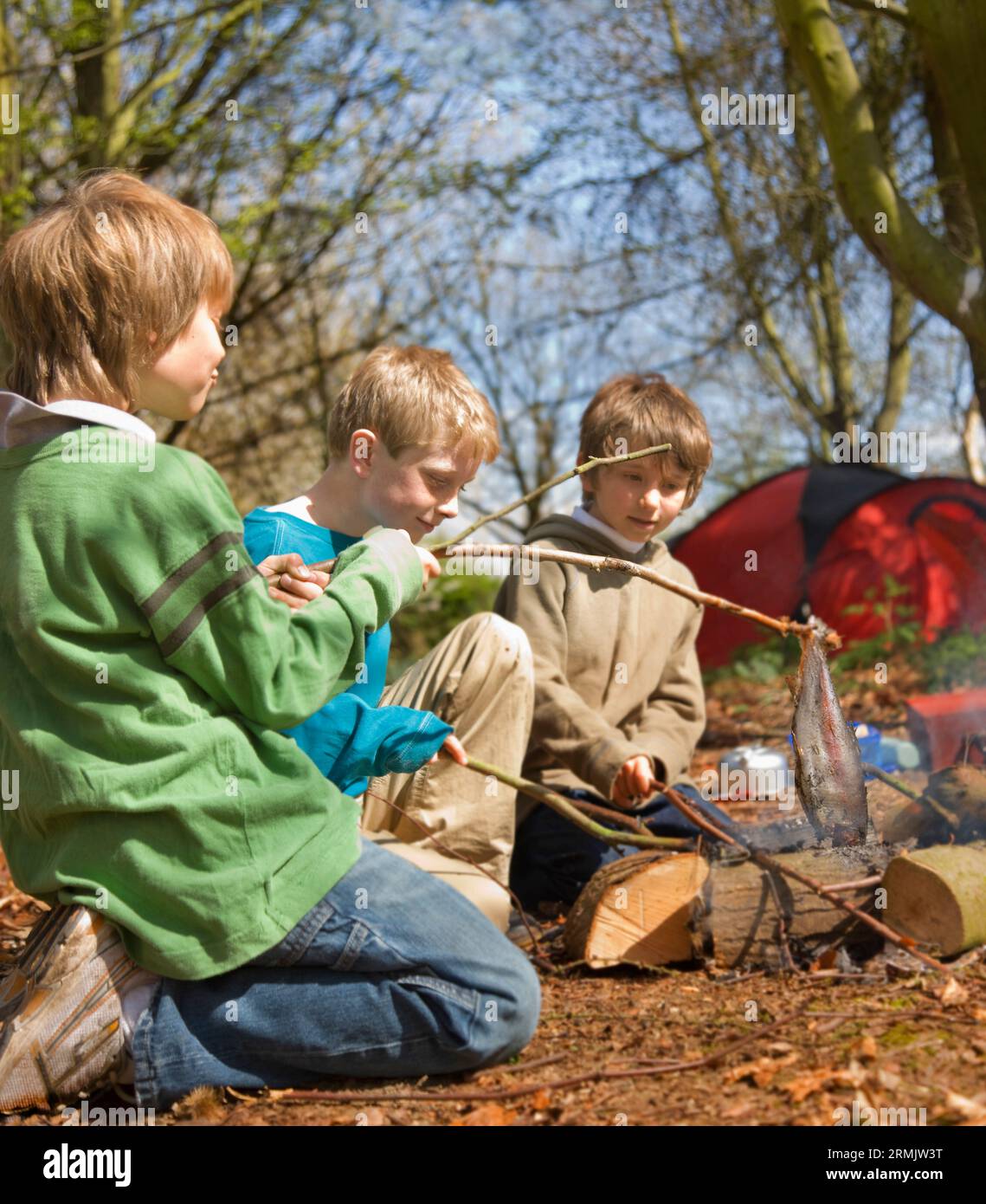 Three boys kneeling around campfire cooking fish Stock Photo - Alamy