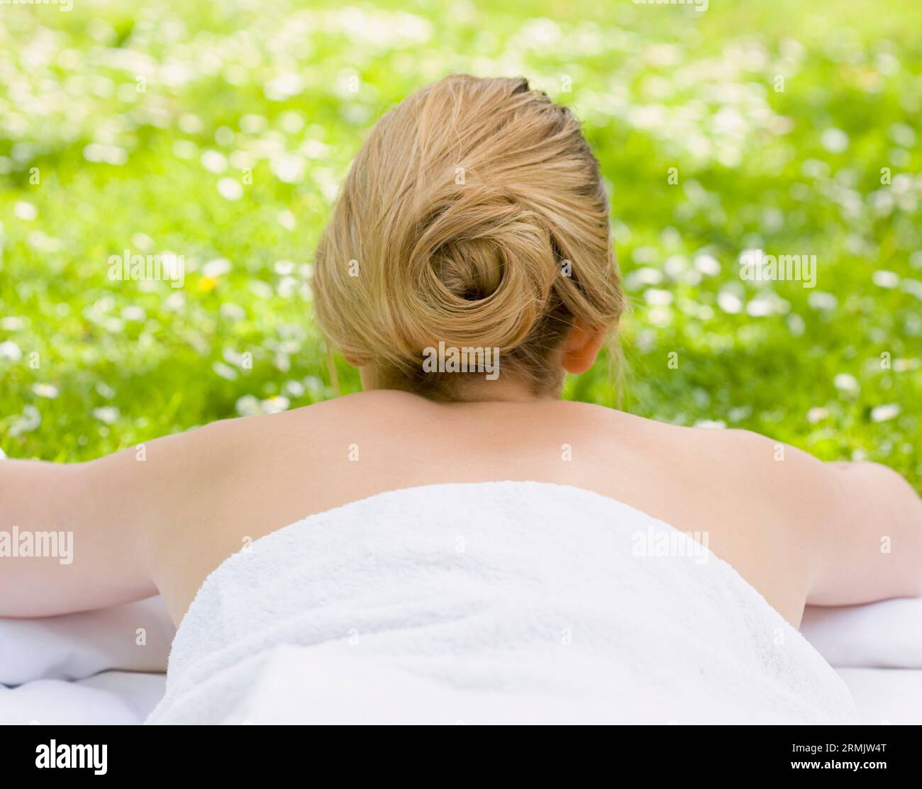 Back view of woman lying on stomach on the grass wrapped in a towel ...