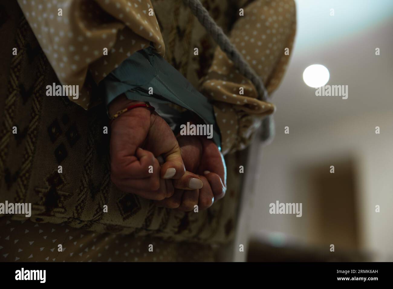 Woman hands tied with a rope. Captive sitting on a chair in the ...