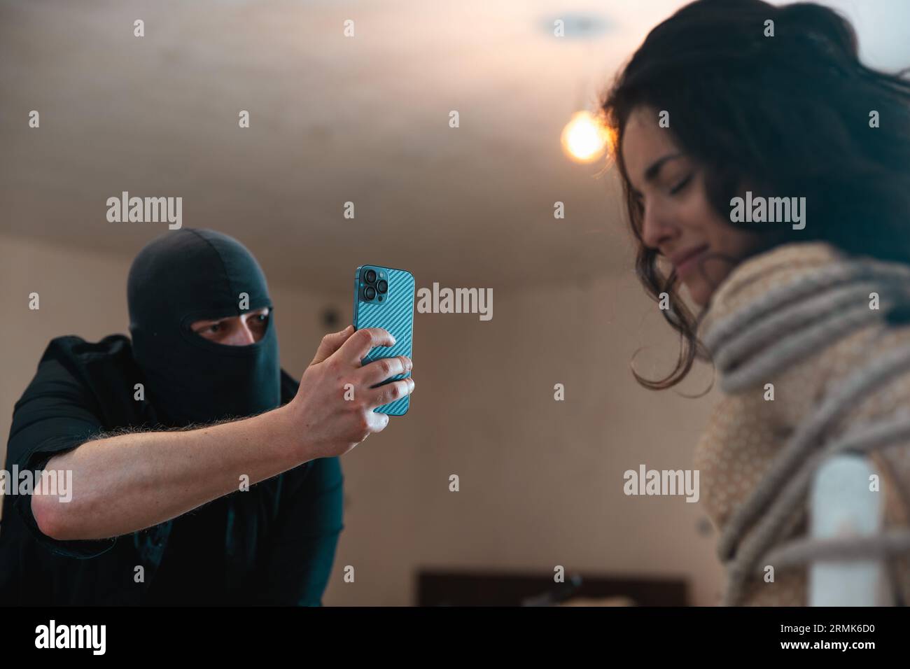 Male kidnapper holding smartphone and filming video of kidnapped woman ...