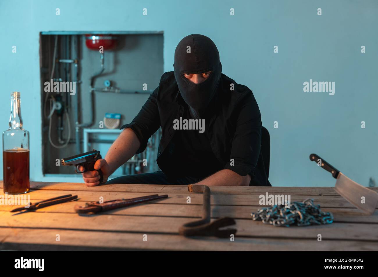Terrible kidnapper in a black balaclava and clothes sitting at a table ...