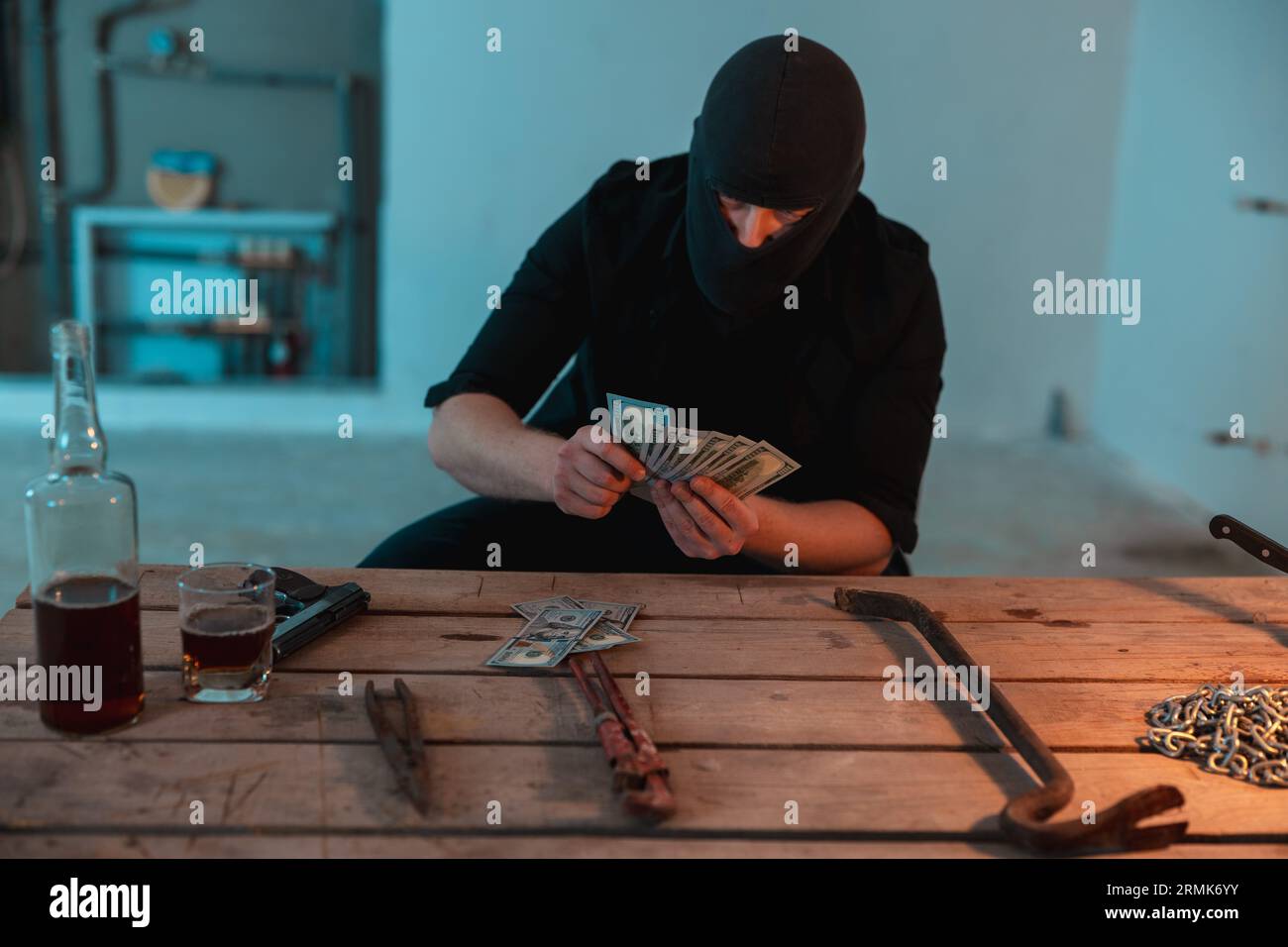 Robber in a black balaclava counting money in the basement. Gun and ...