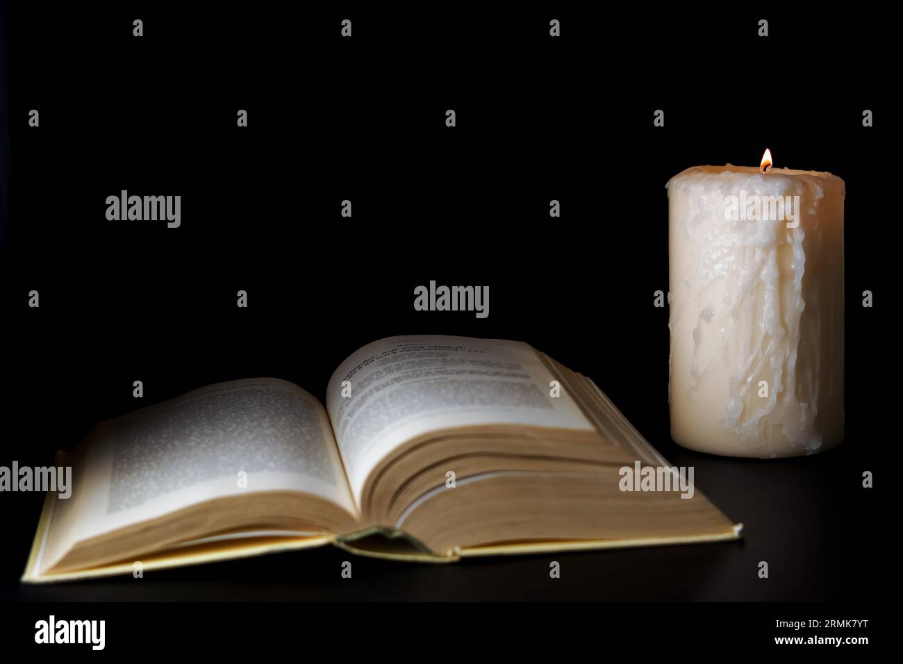 Open book illuminated by candlelight isolated on a black background ...