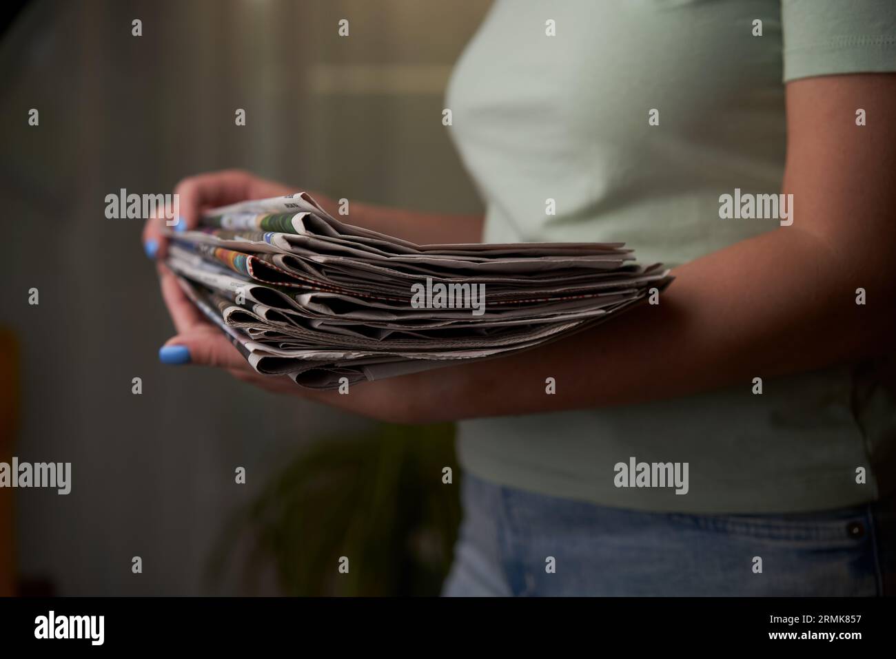 A woman stacks old newspapers in a pile, waste paper collect. Preparing ...