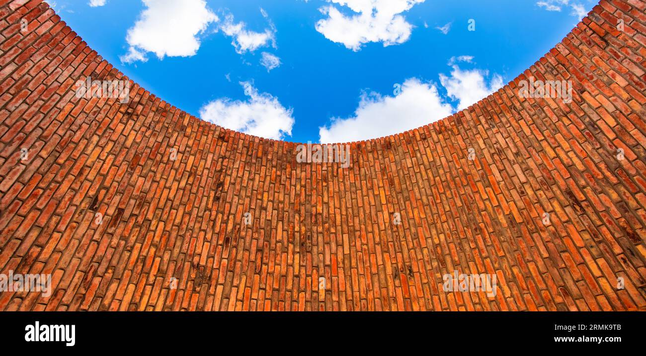 A circular brick wall structure with a blue sky with white clouds in ...