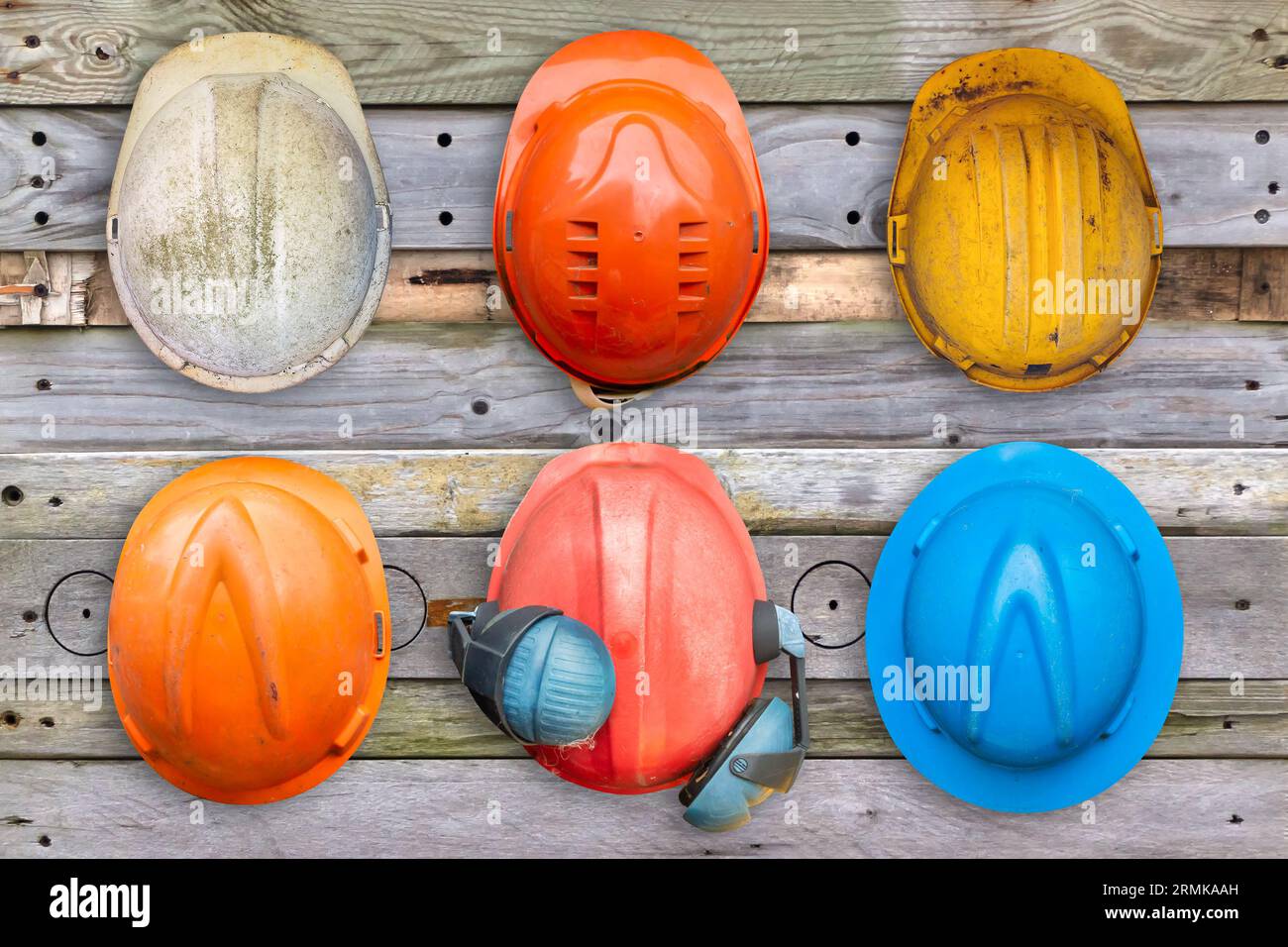 Six colorful old and worn construction helmets hanging on a wooden wall ...