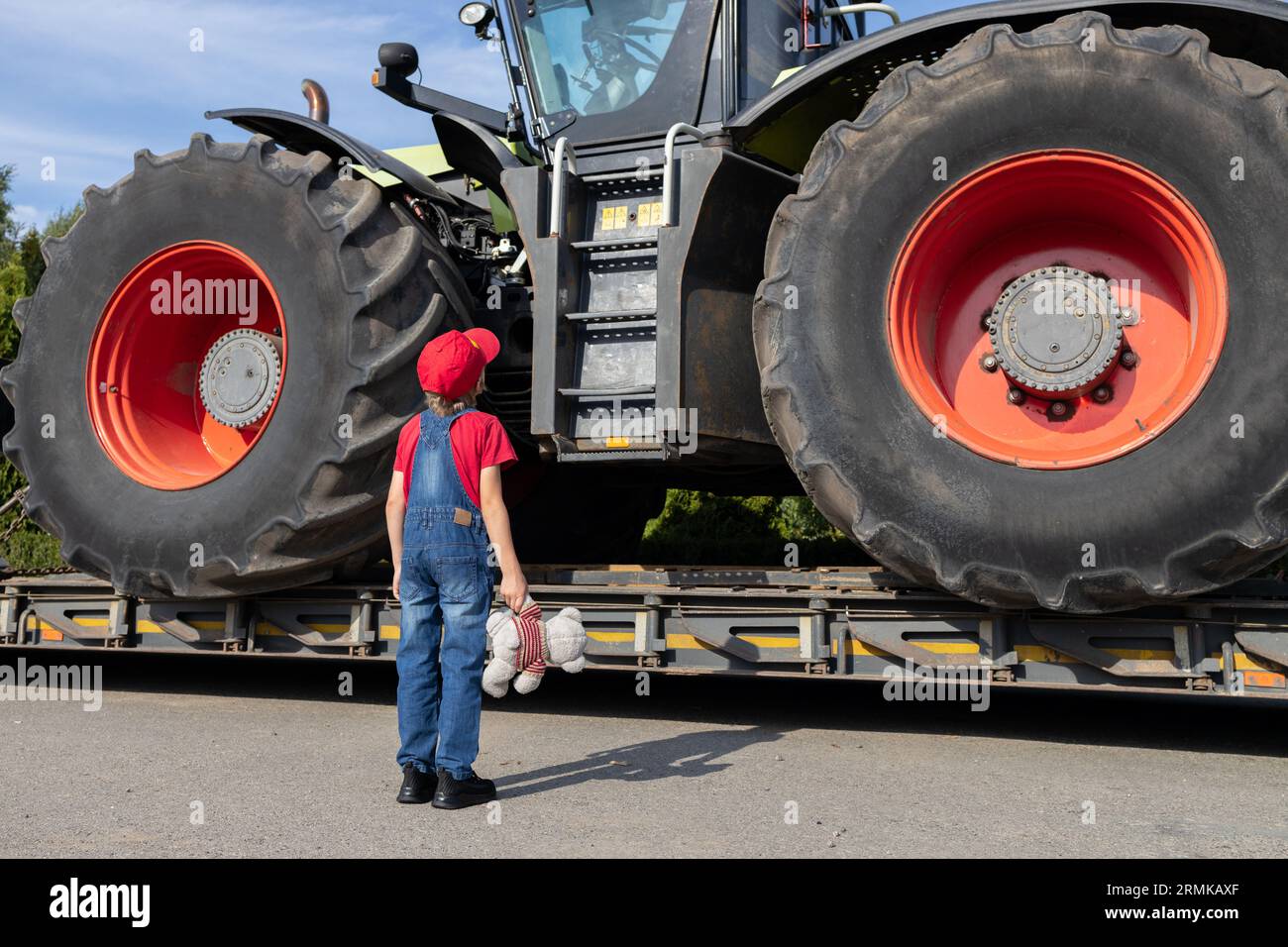boy in denim overalls stands with his back in the frame and examines a ...