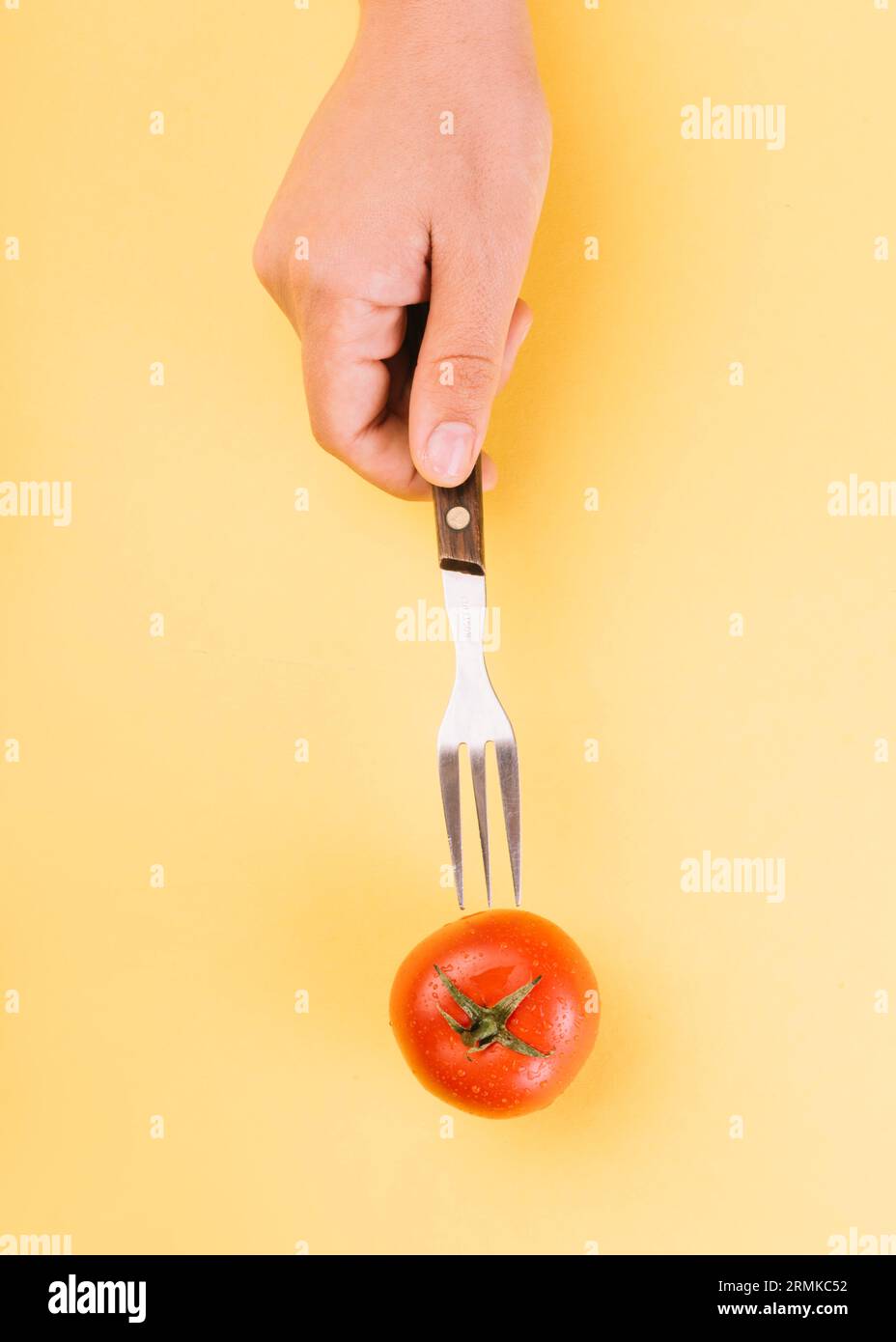 Human hand inserting fork red tomato yellow backdrop Stock Photo - Alamy