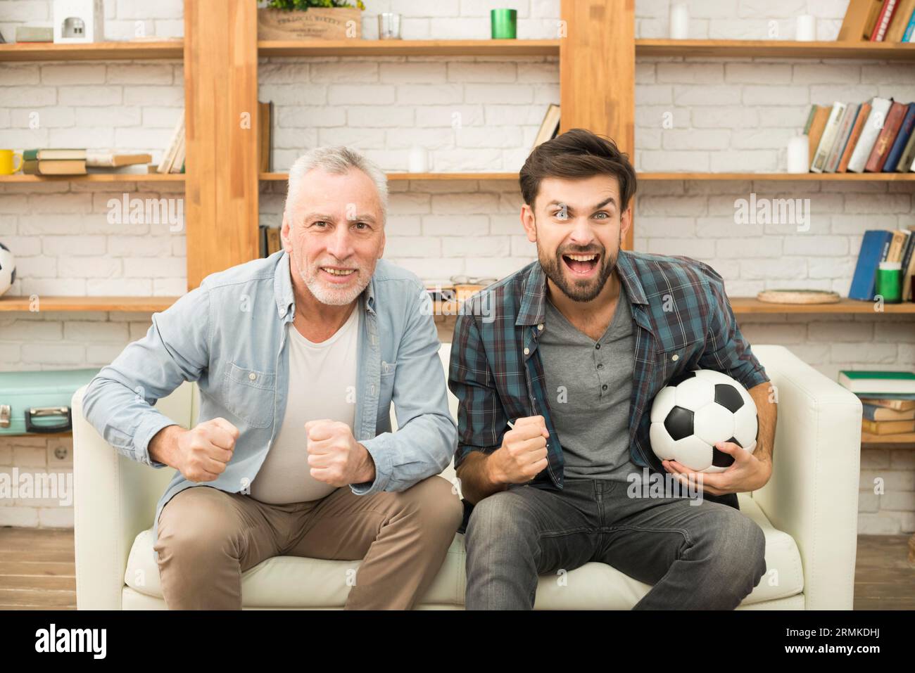 Aged man young crying guy with ball watching tv sofa Stock Photo - Alamy