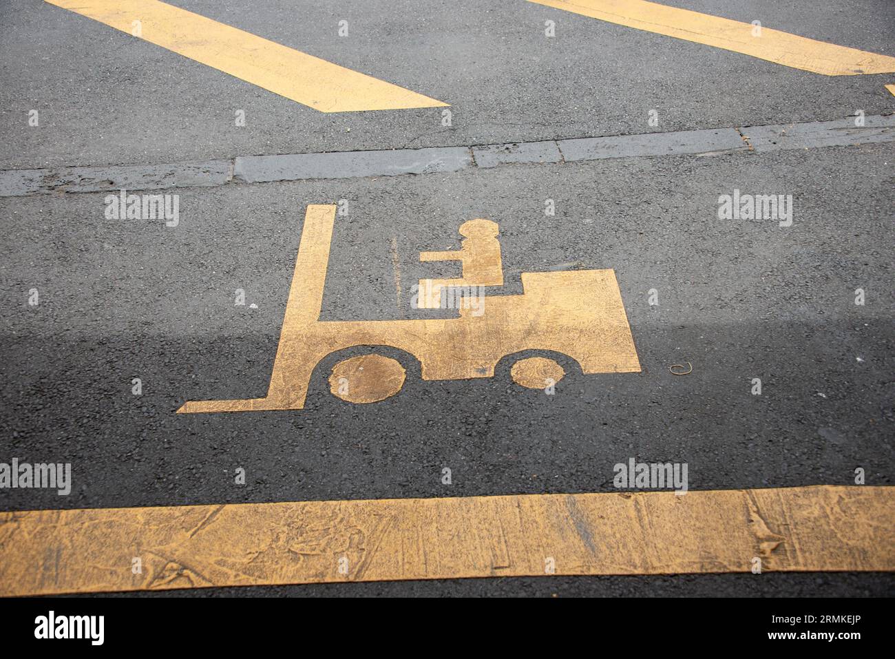 A yellow forklift safety symbol on black asphalt road indicating ...